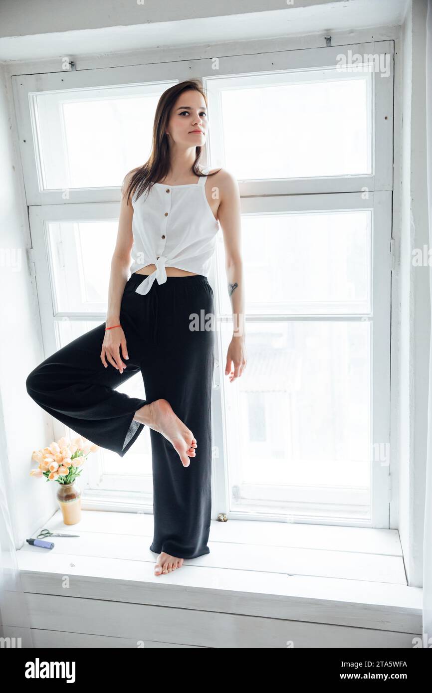 Portrait of a beautiful fashionable woman at the window in a white room ...