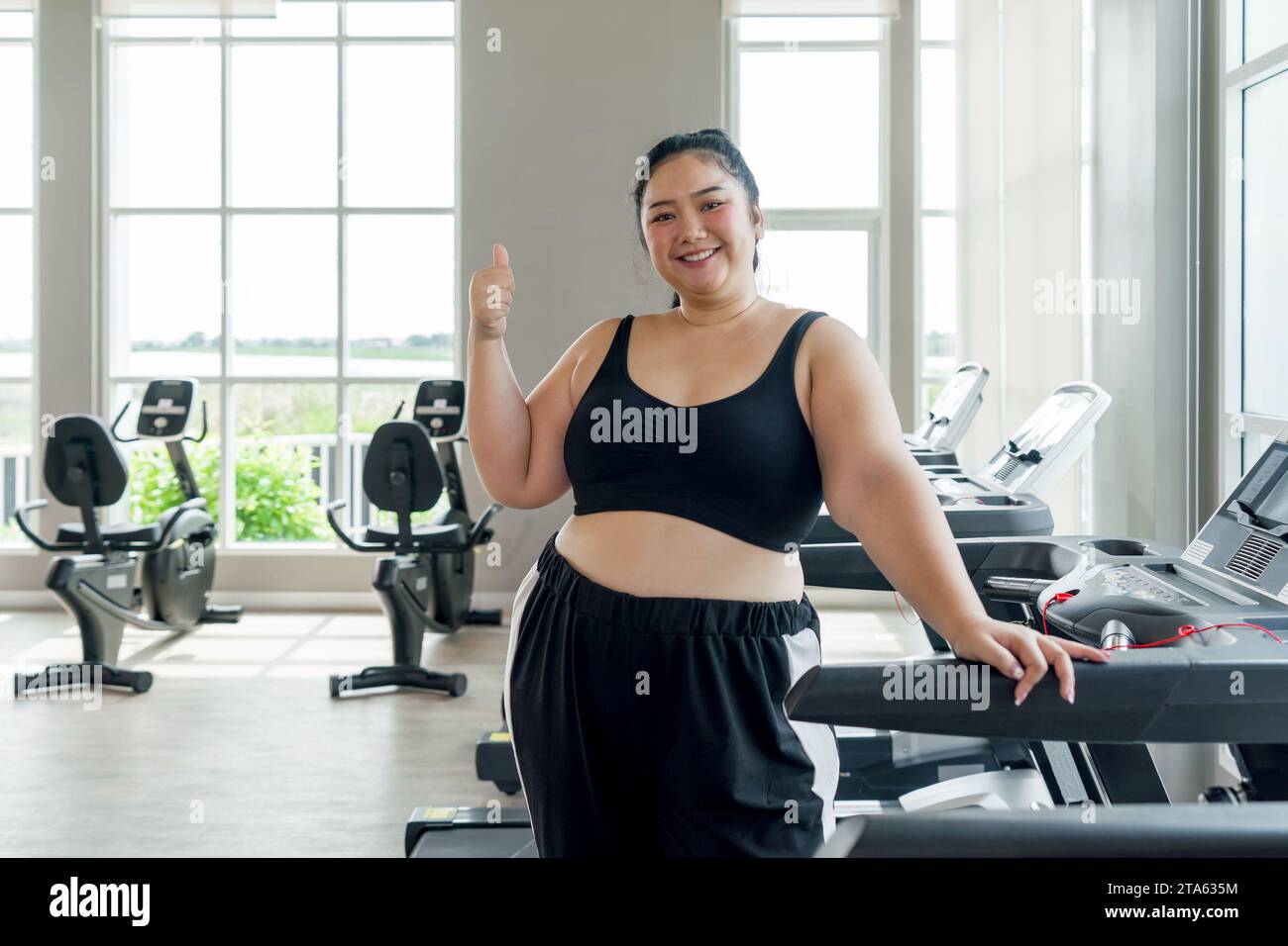 A plus-sized woman is standing on a treadmill in a gym, preparing to ...