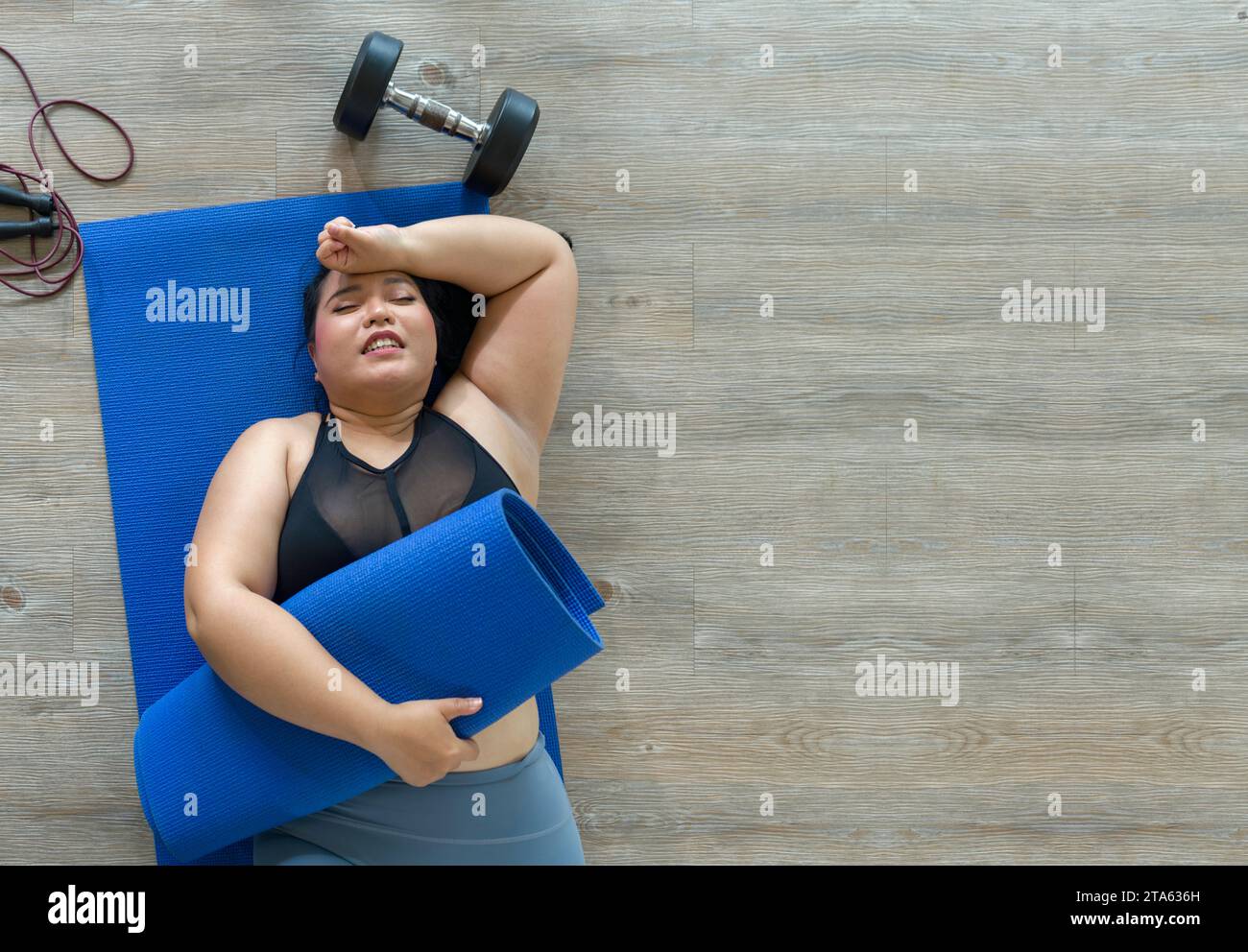 A plus-size woman lies exhausted on a blue mat, taking a breather after ...