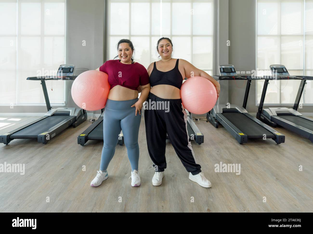 Two plus-sized women are standing in front of a treadmill in a gym ...