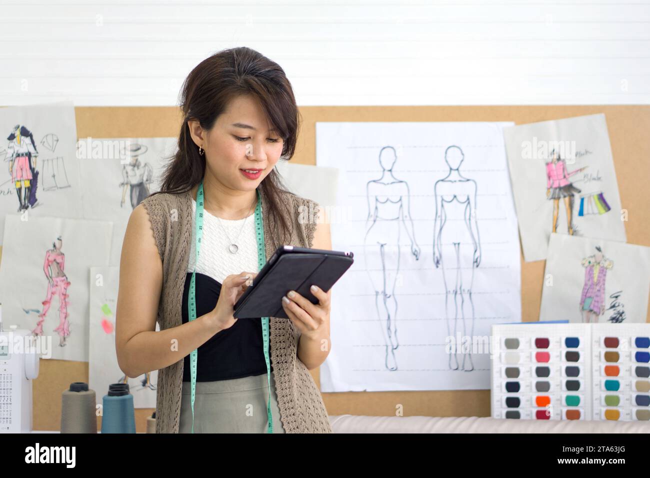 Young asian dressmaker checking email order from tablet computer ...