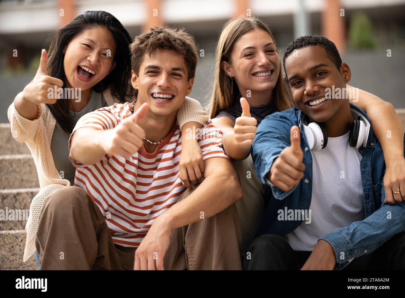 Cheerful multicultural group of friends showing thumbs up sitting on ...