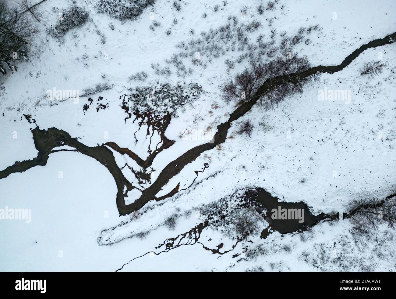 Schmitten, Germany. 29th Nov, 2023. A stream meanders through the snow ...