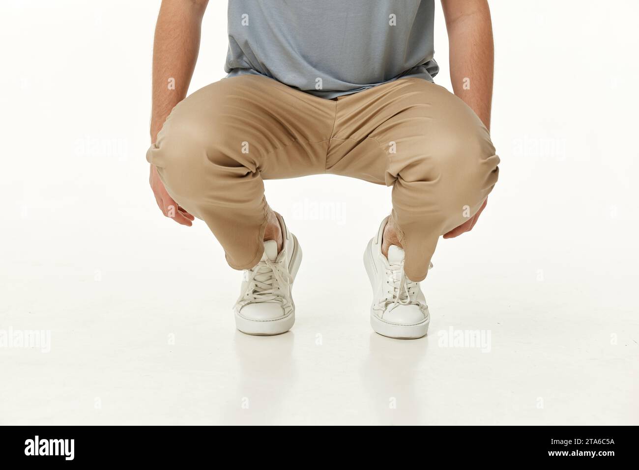 man wearing white sneakers and casual beige pants squatting on studio ...