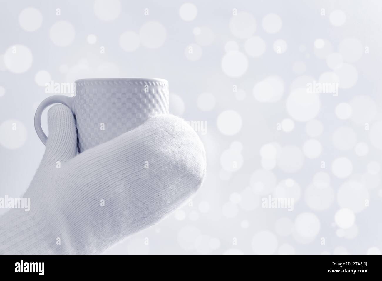 Mittened hands hold white mug with warm drink on wite background with ...