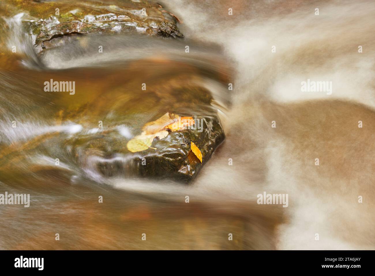 The water of a fast-flowing river splashes around and over a mid-stream ...