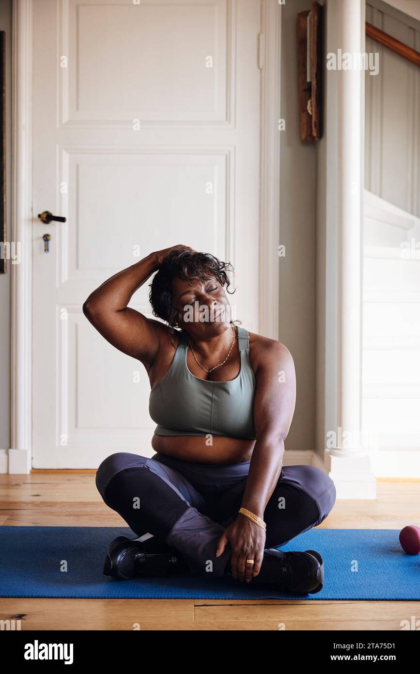 Mature woman with eyes closed practicing relaxation exercise on mat at ...