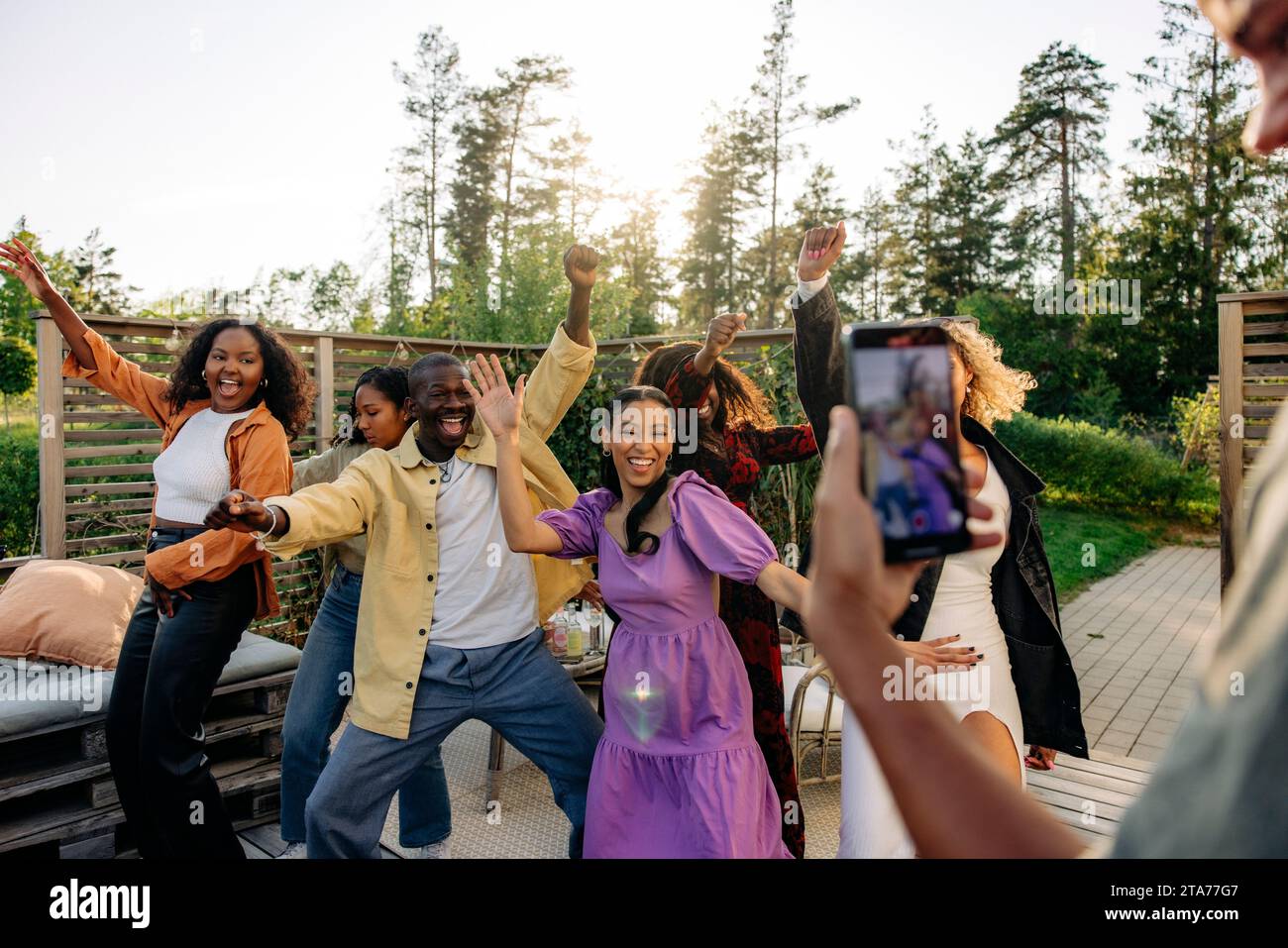 Man photographing cheerful male and female friends dancing during party ...