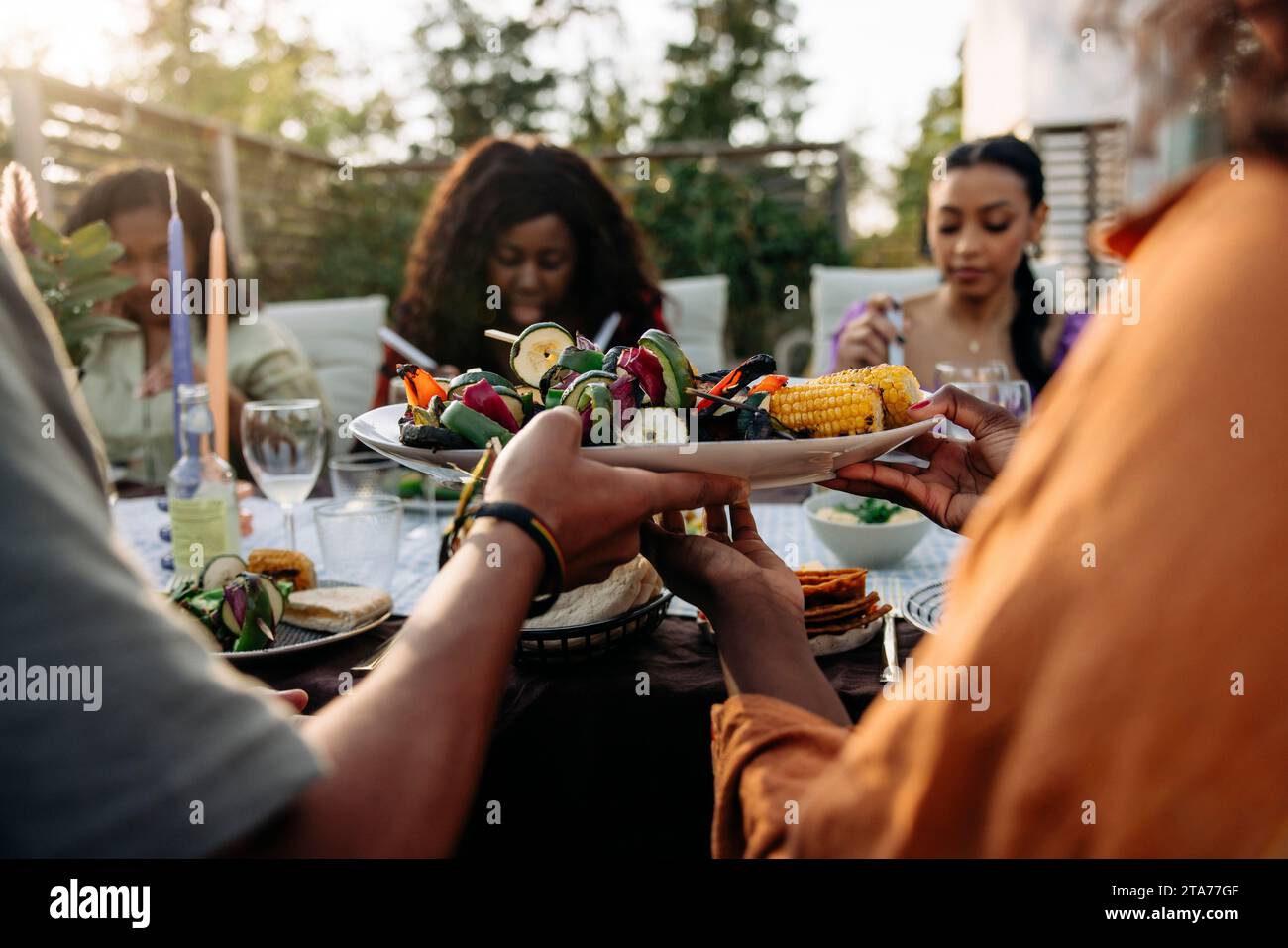 Friends passing snacks plate to each other during dinner party in back ...