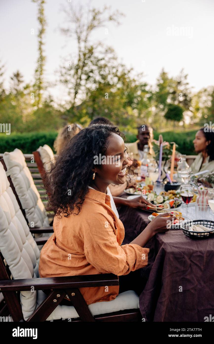 Side view of happy woman laughing while having food with friends at ...