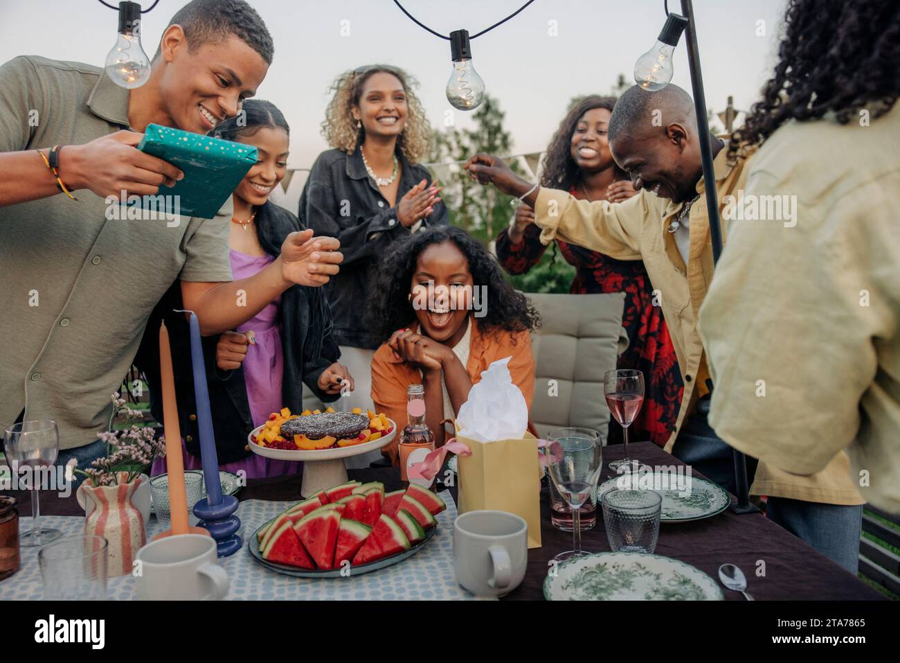 Happy friends giving gifts to excited young woman while celebrating ...