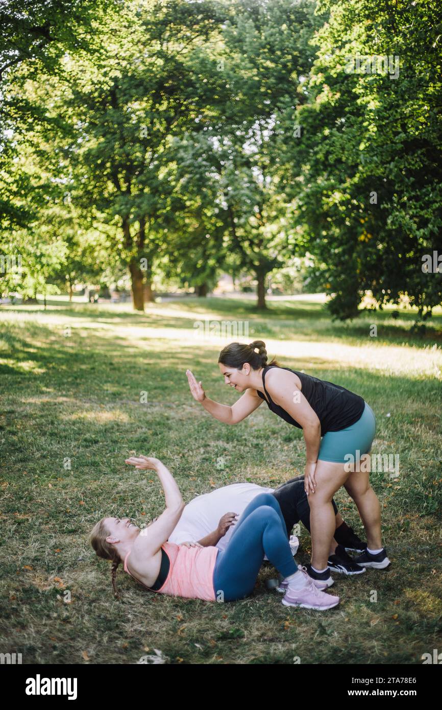 Side view of female coach giving high-five to woman lying on grass at ...