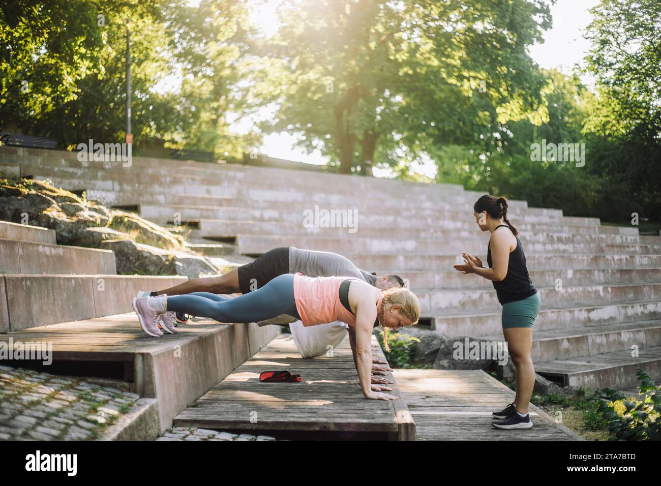 Side view of female instructor motivating team while doing push-ups on ...