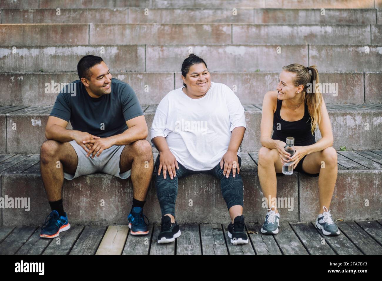 Smiling male and female workout buddies talking to each other while ...