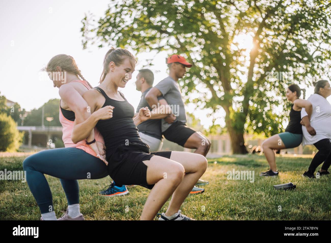 Smiling multiracial male and female friends doing buddy back stretch on ...