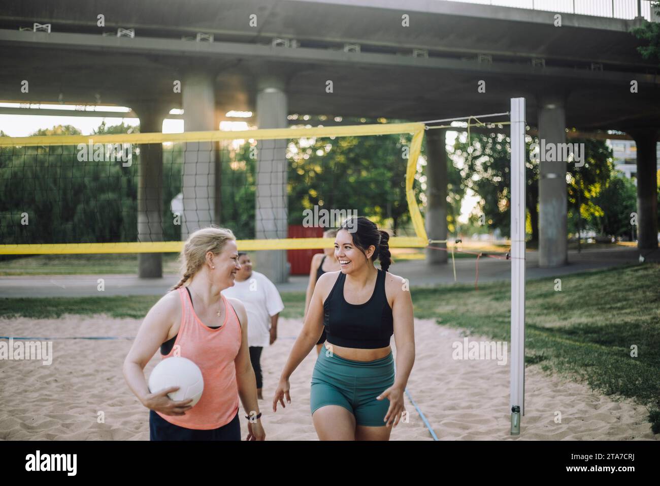 Smiling female friends walking while playing volleyball Stock Photo - Alamy