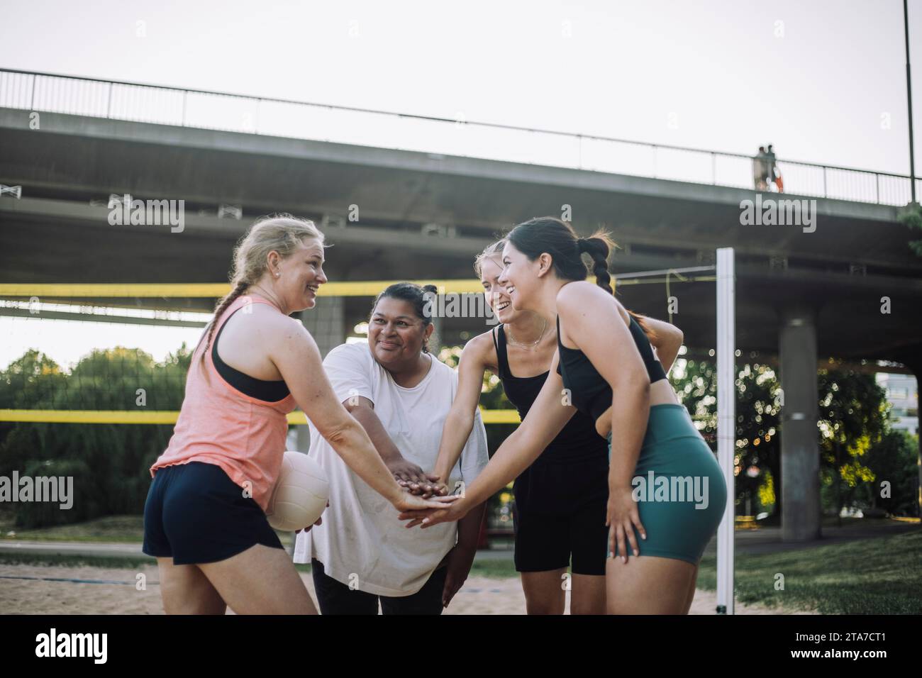 Smiling female friends stacking hands while playing volleyball Stock ...