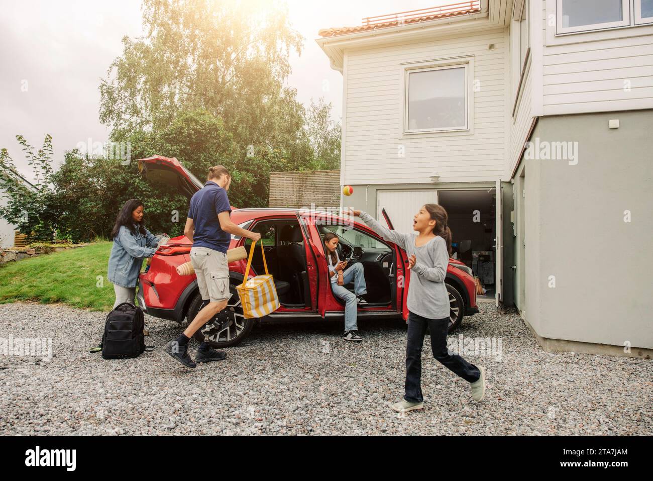 Girl playing with ball near family loading stuff in electric car by ...