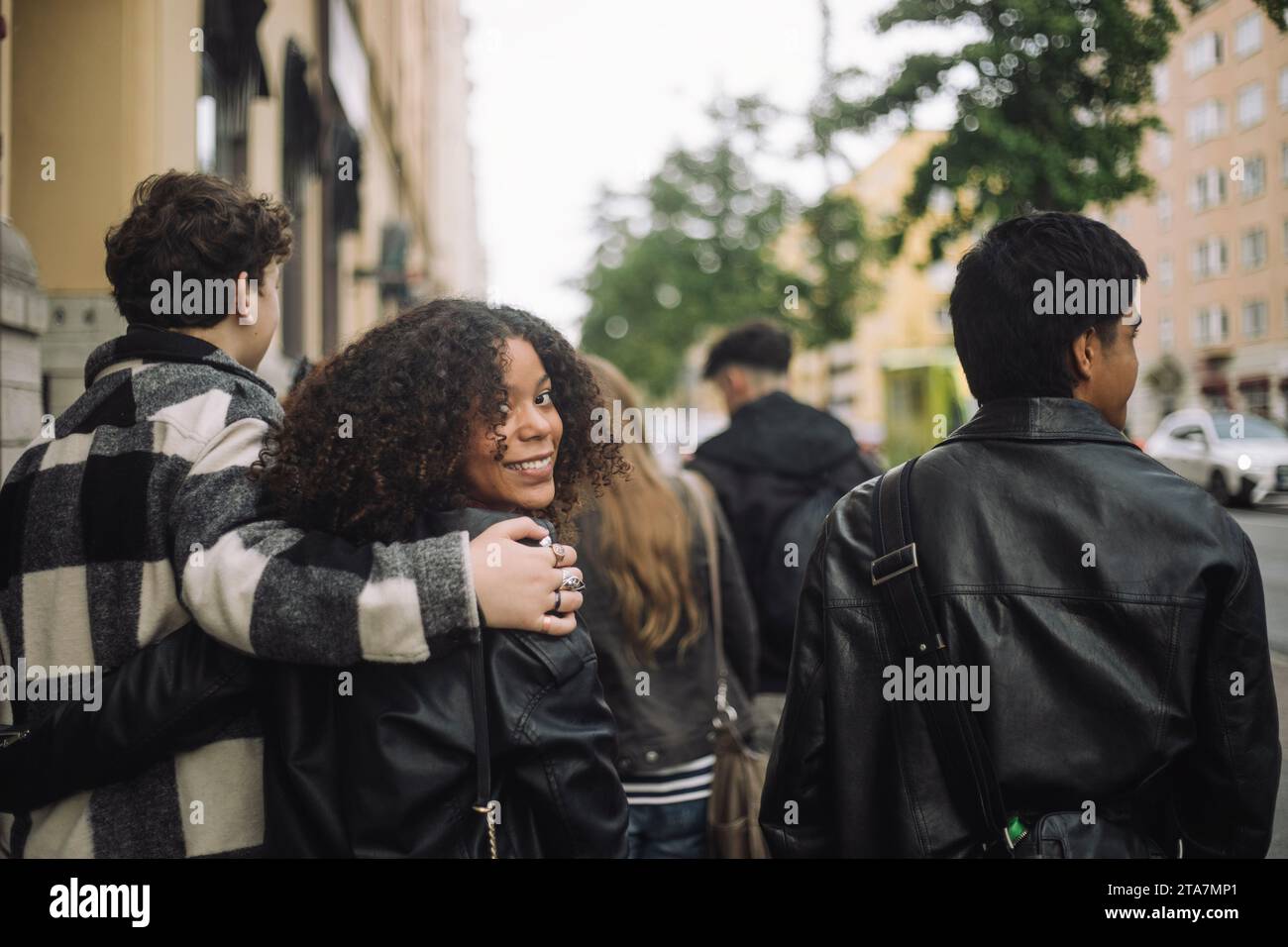 Boy with arm around female friend looking over shoulder while walking ...