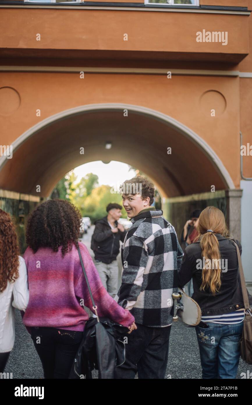 Smiling teenage boy looking over shoulder while walking with friends ...