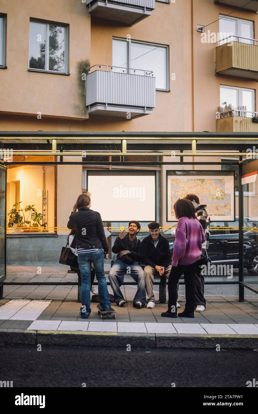 Happy male and female friends having fun at bus stop in city Stock ...