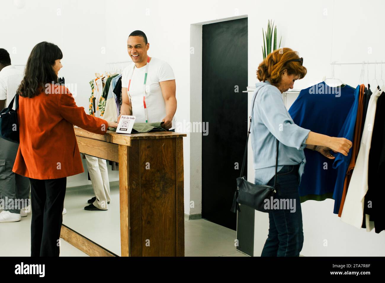 Smiling male tailor talking with customer standing near table at store ...