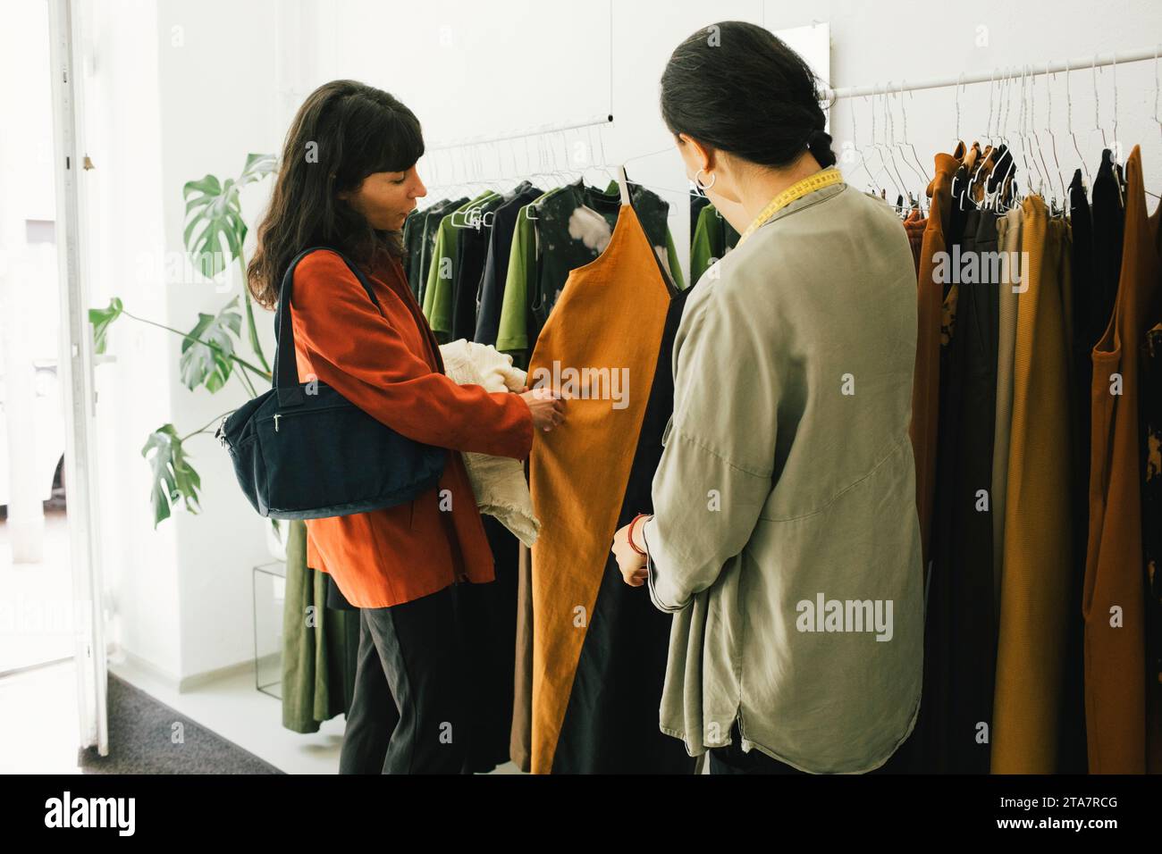Female sales staff assisting woman while choosing dress from rack at ...