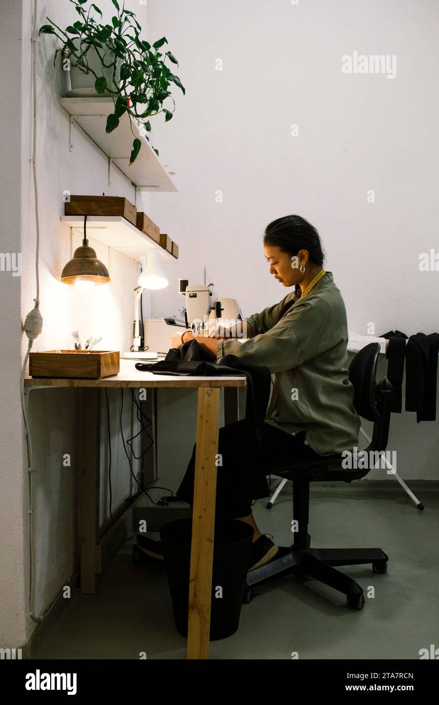 Side view of seamstress stitching clothes using sewing machine while ...