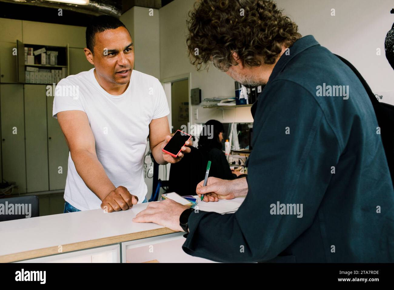 Mature repairman showing broken smart phone to customer doing paperwork ...