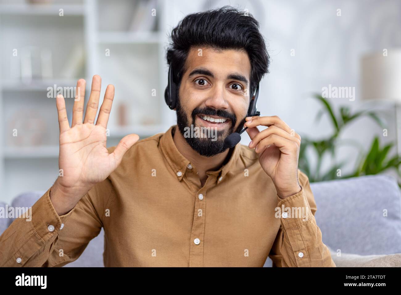 Camera view of positive smiling indian man with wireless headset waving ...