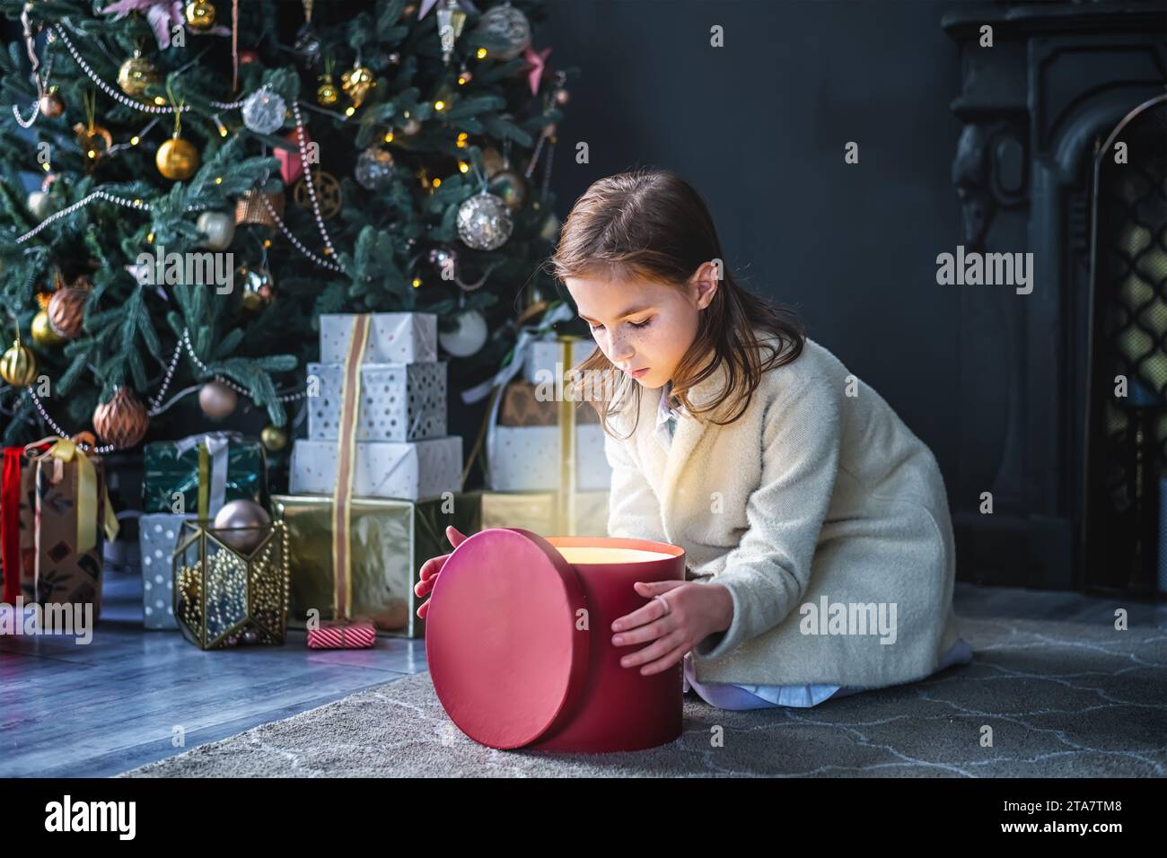 Cute girl opening Present next to Cristmas Tree. Happy Girl looking ...