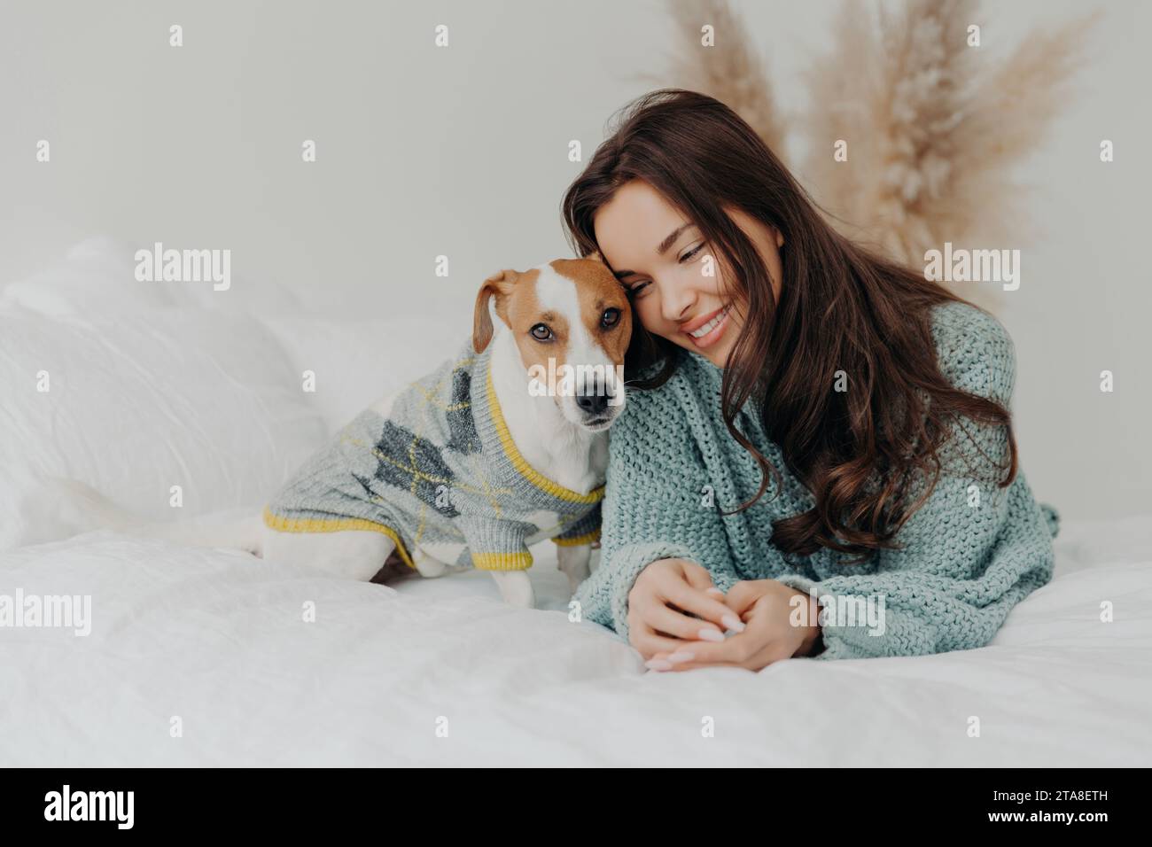 Woman in a cozy sweater cuddling her dog on the bed, sharing a moment ...