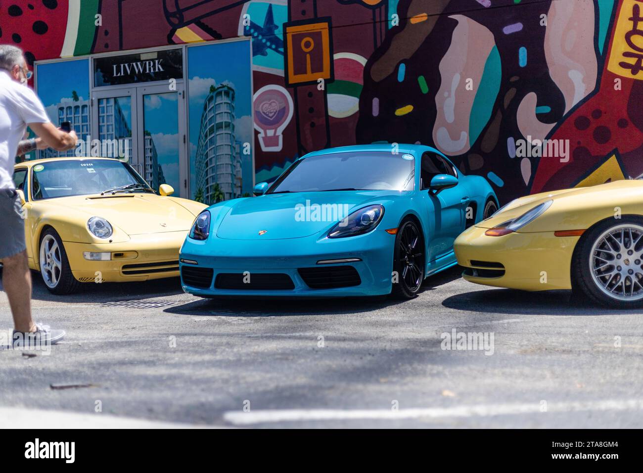 Brightly colored Porsche sports cars parked near a mural in an arts ...
