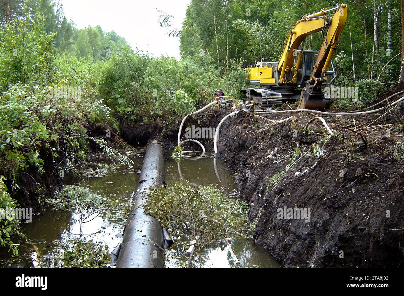 Big yellow excavator near a pit with a gas pipeline. The pit is filled ...