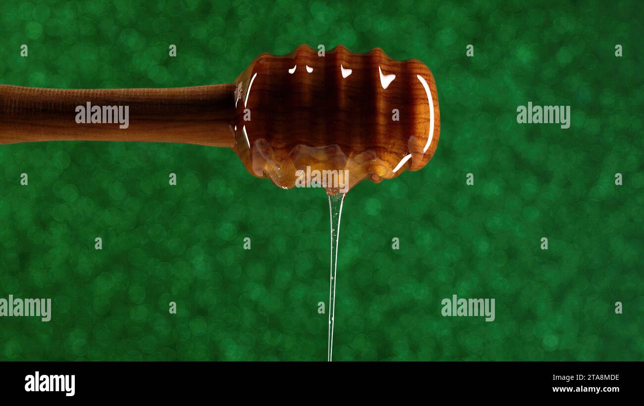 Organic honey flows from wooden dipper stick on green background ...