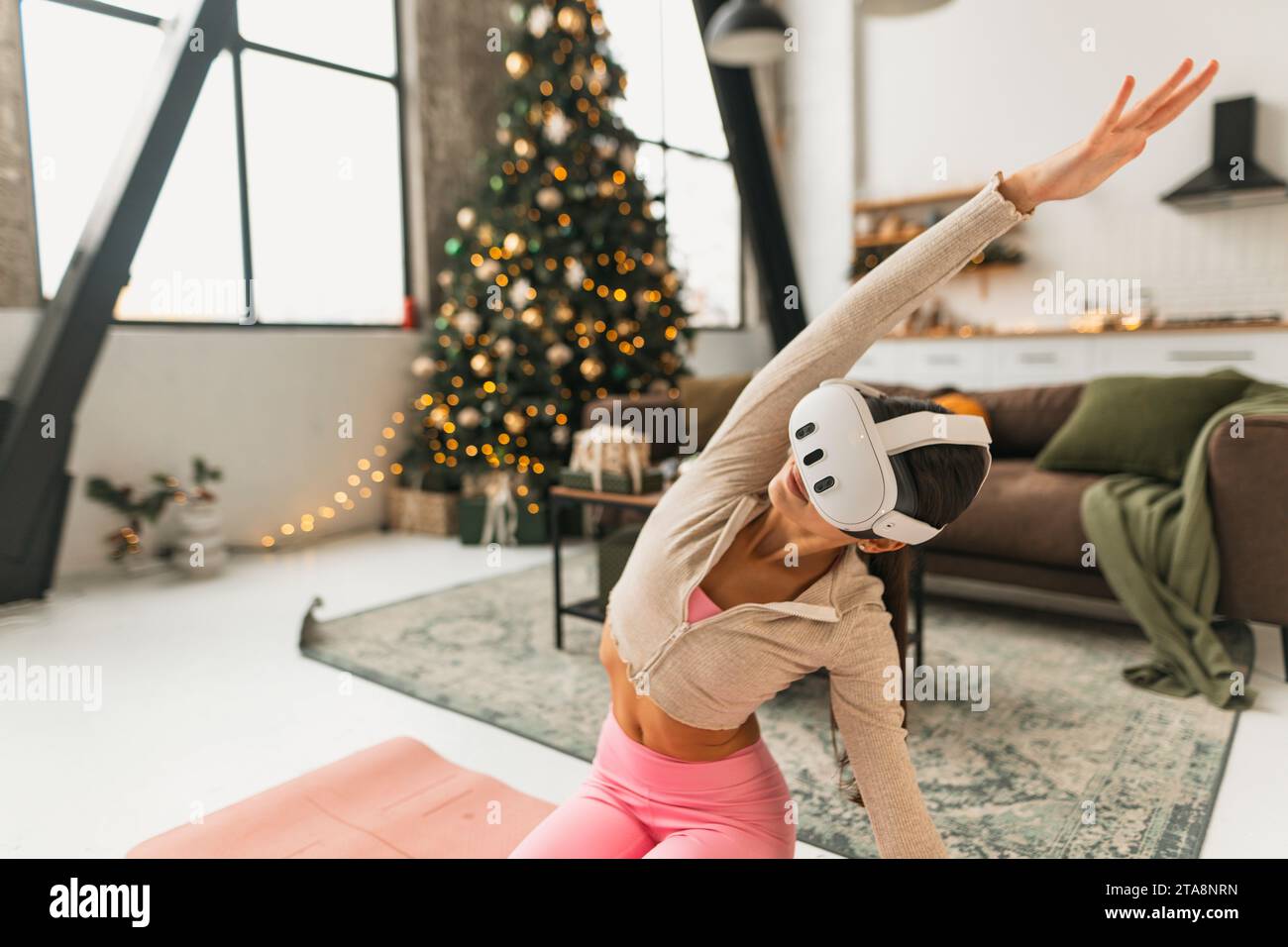 In front of a Christmas tree, a fitness enthusiast performs yoga poses ...