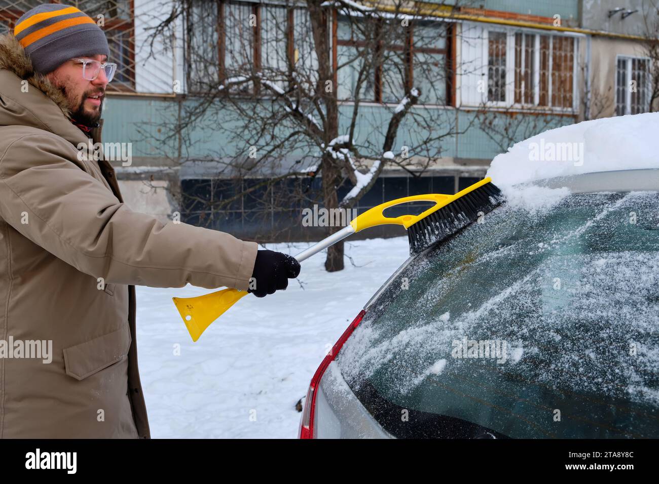 Amidst winter, a man diligently brushes off snow from his car, a ...