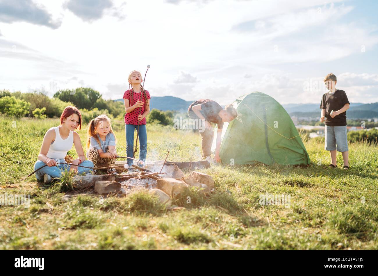 Three sisters cheerfully laughing and roasting marshmallows and candies ...