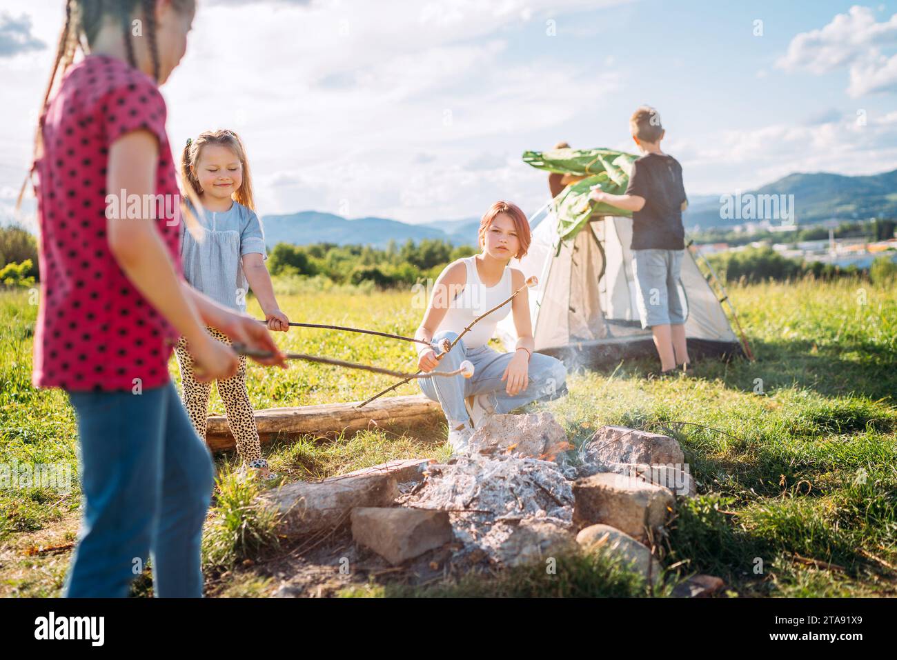 Three sisters have picnic, roasting marshmallows and candies on sticks ...