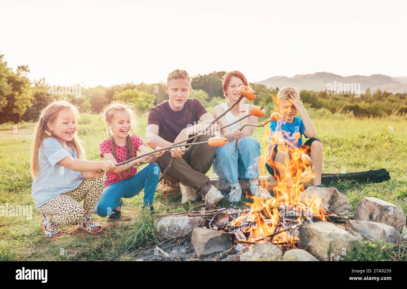 Five kids group Boys and girls cheerfully laughed and roasted sausages ...