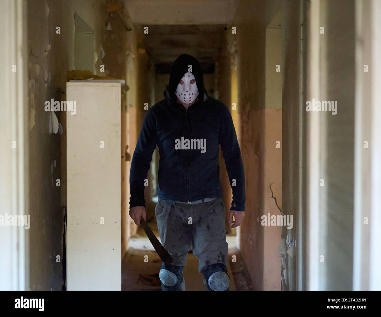 A man in a hockey mask with a machete in his hand walks down a shabby ...