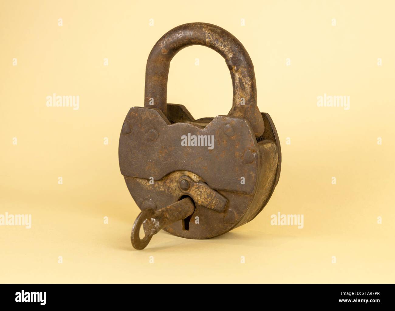 An old rusty padlock with a key in the middle on a beige background ...