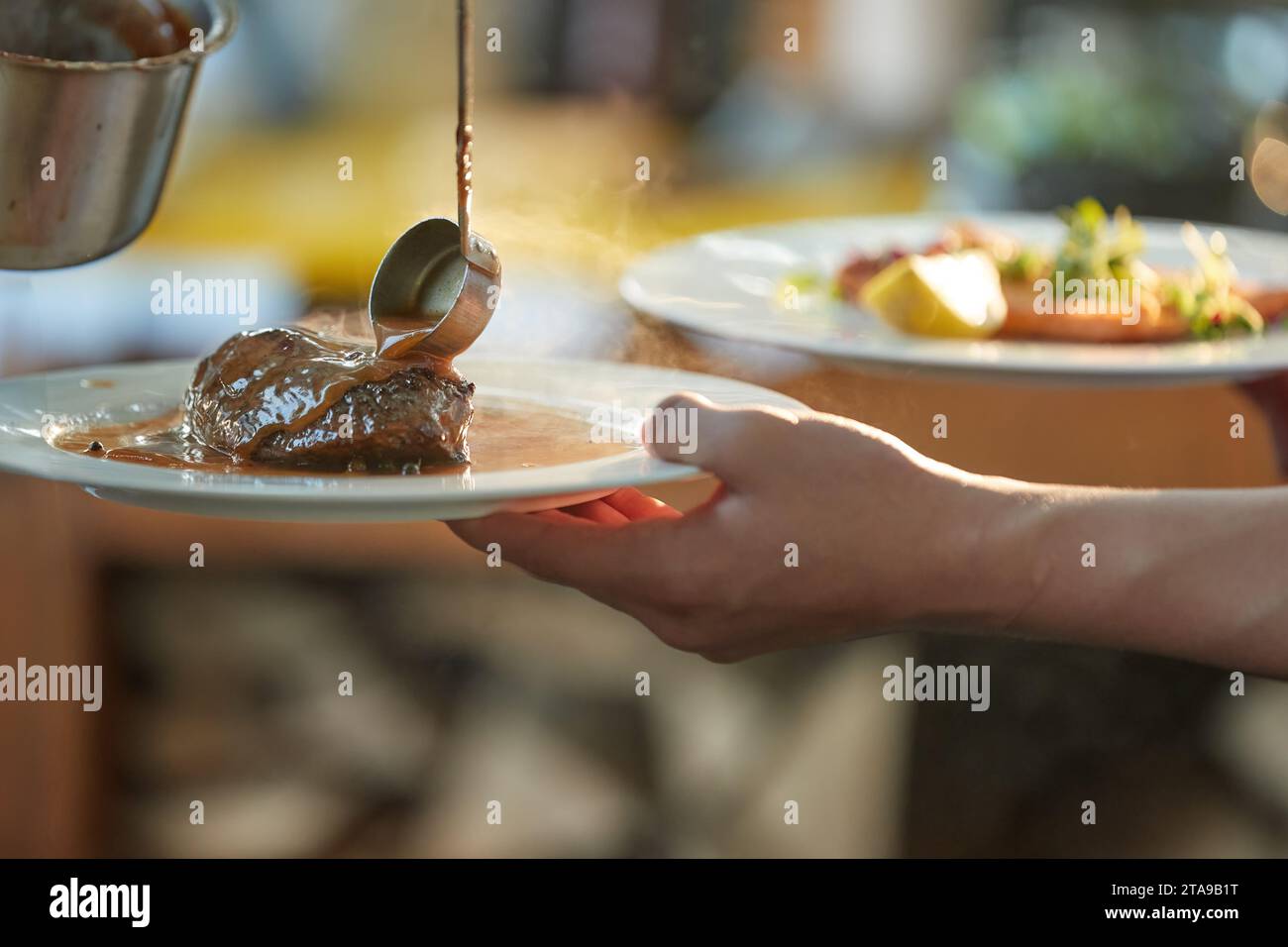 Chef pouring sauce over steak. Close up of cooking at garden party. Two ...