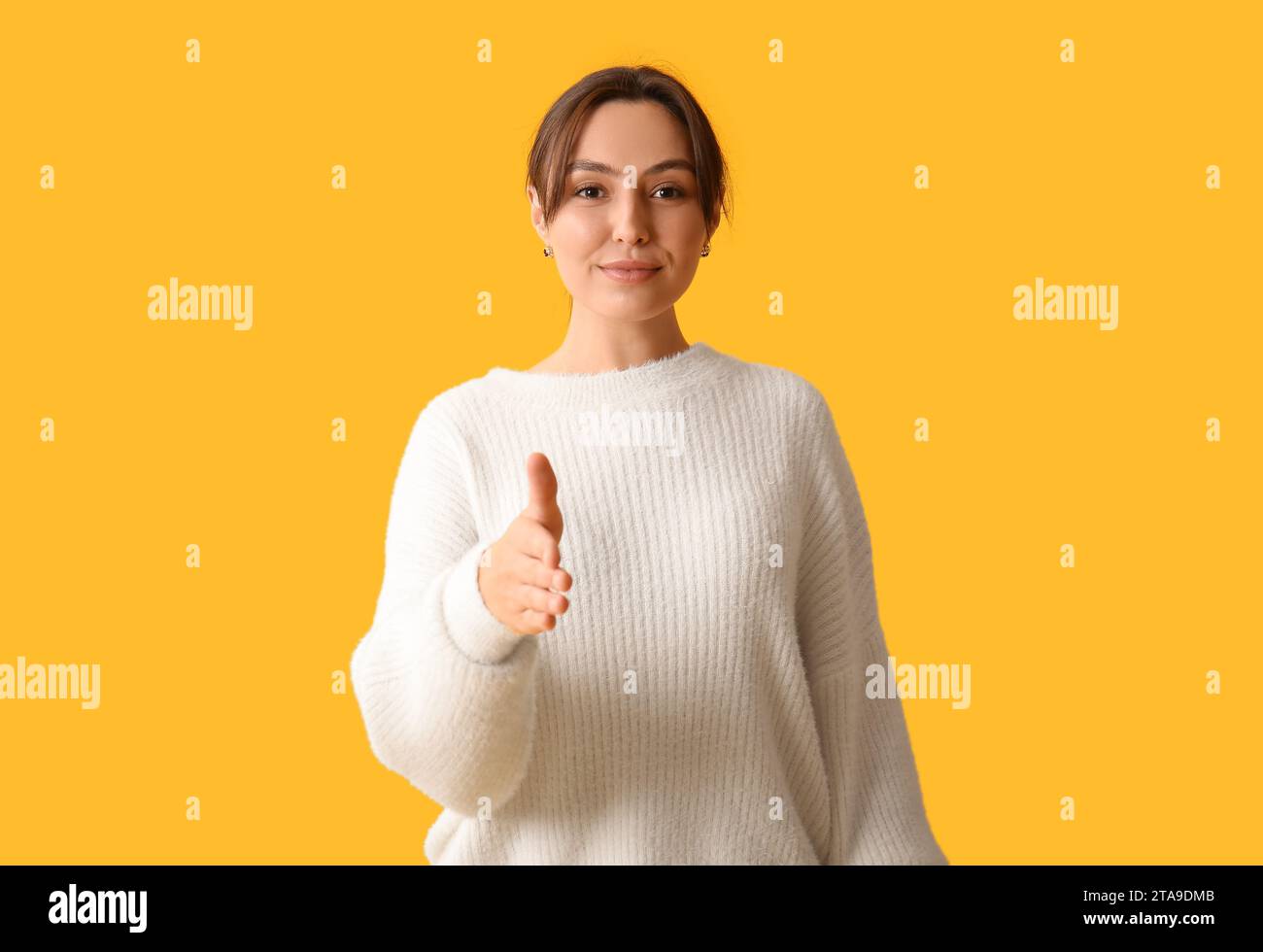 Beautiful young woman extending hand for handshake on yellow background ...