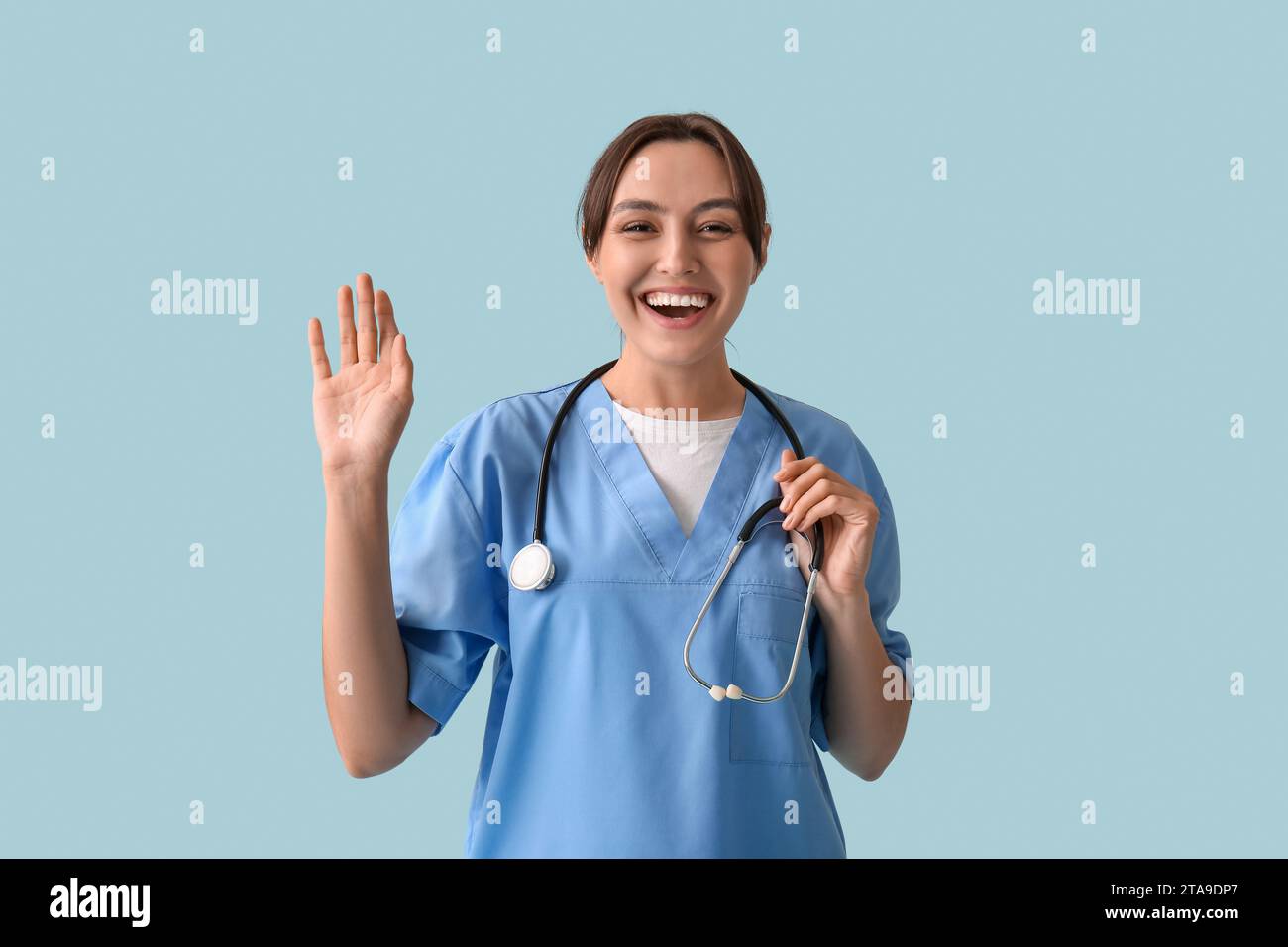 Beautiful female doctor waving hand on blue background Stock Photo - Alamy