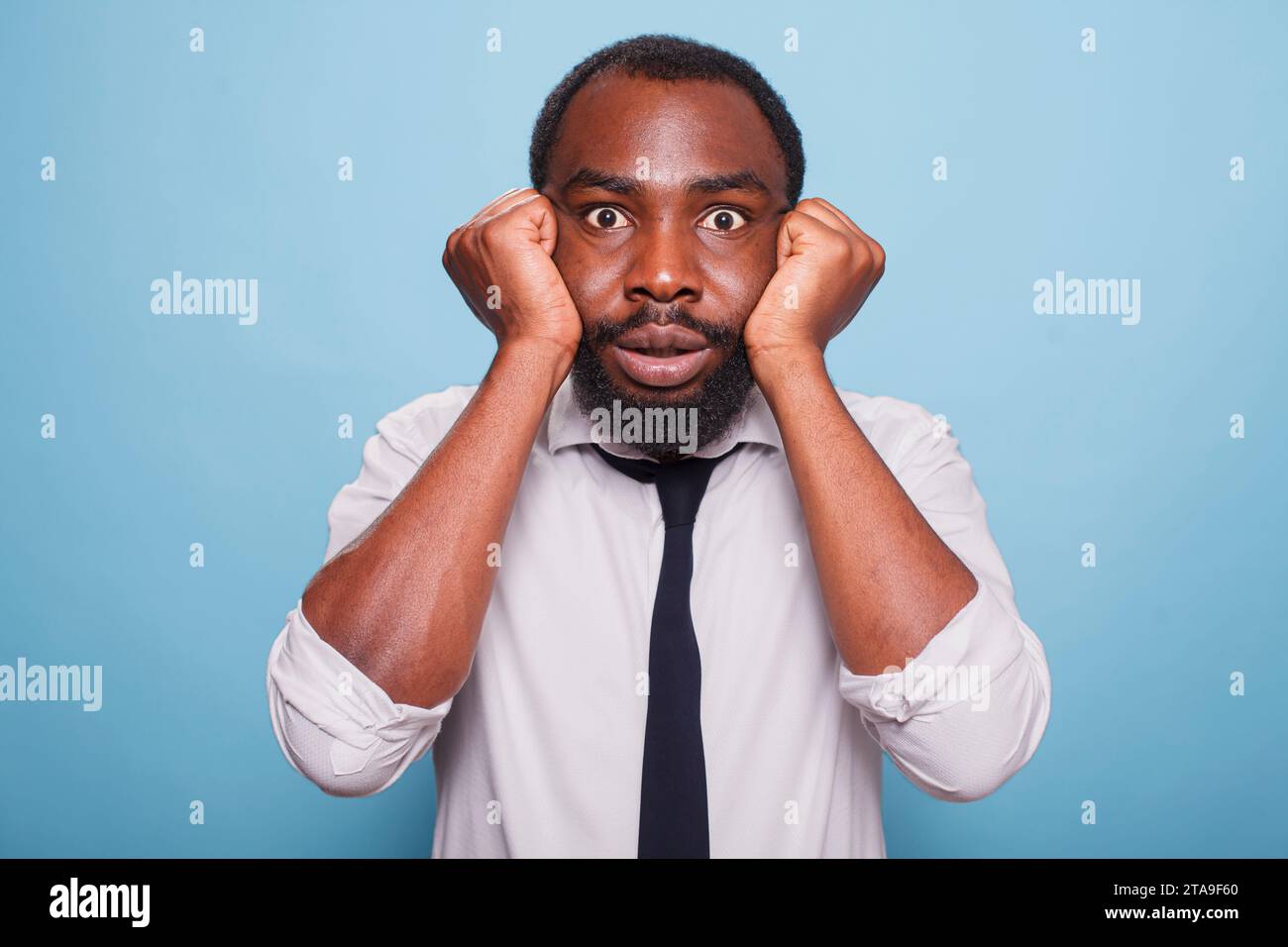 Over a blue background, a nervous entrepreneur with open eyes holds his ...