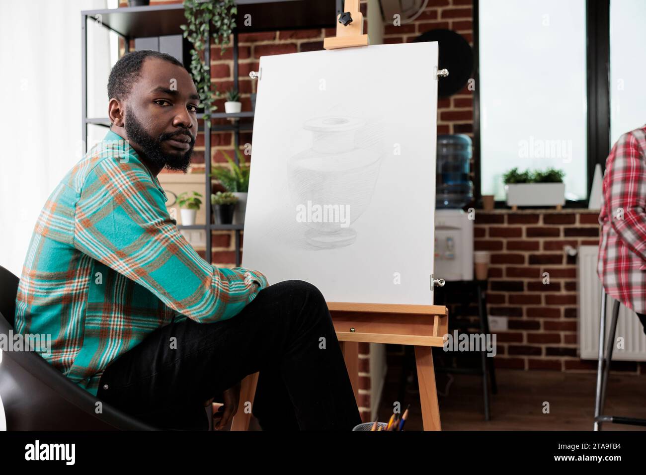 African American guy sitting at easel in classroom and looking at ...