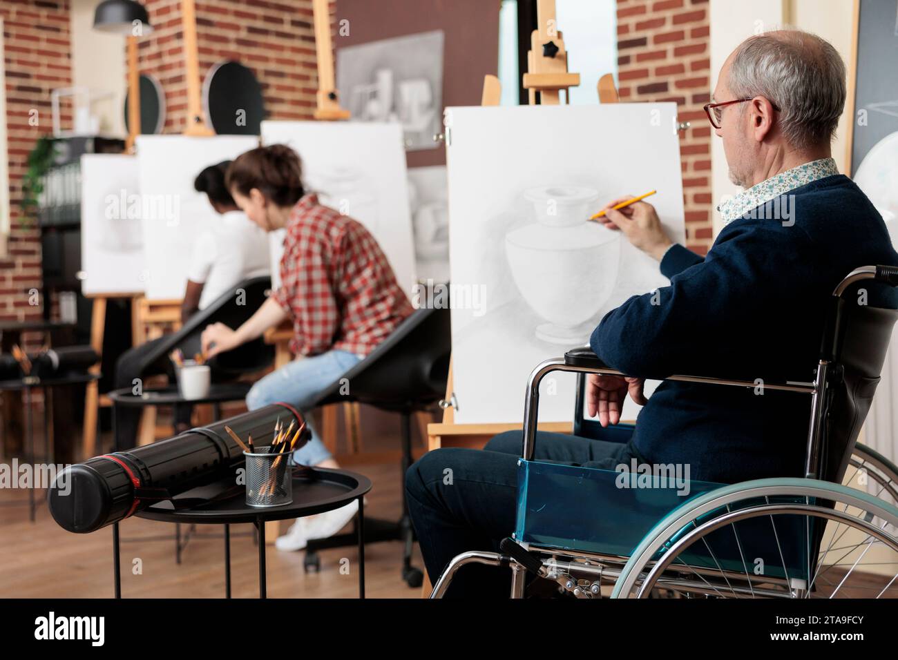 Senior man with physical disabilities sitting at easel during group art ...