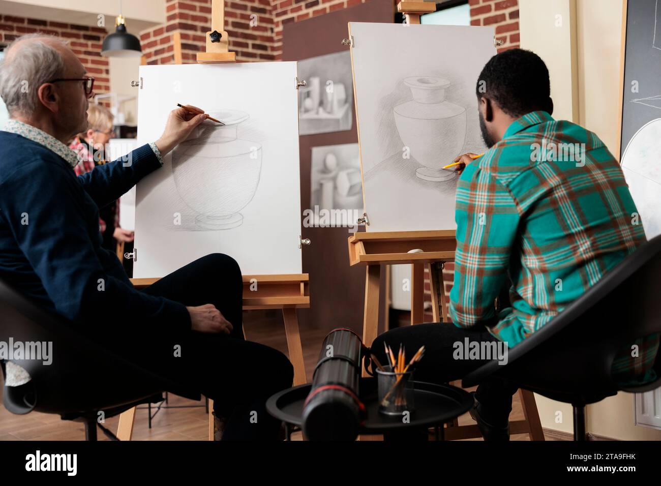 Rear view of two diverse men students sitting at easels practicing ...
