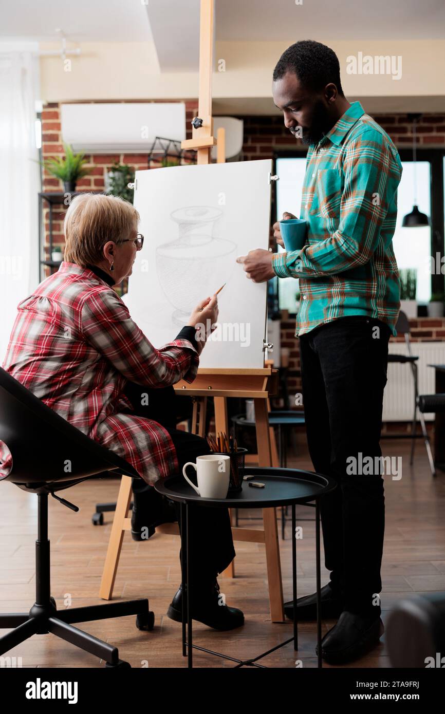 African American guy art instructor teaching senior woman to draw in ...
